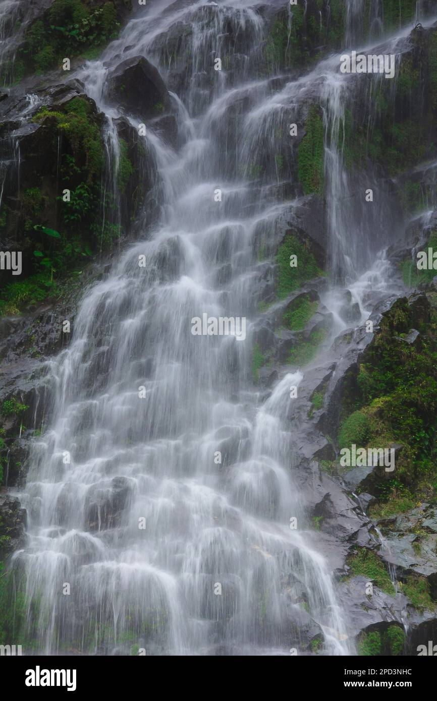 A natural waterfall flows down a long line from a cliff into a ...