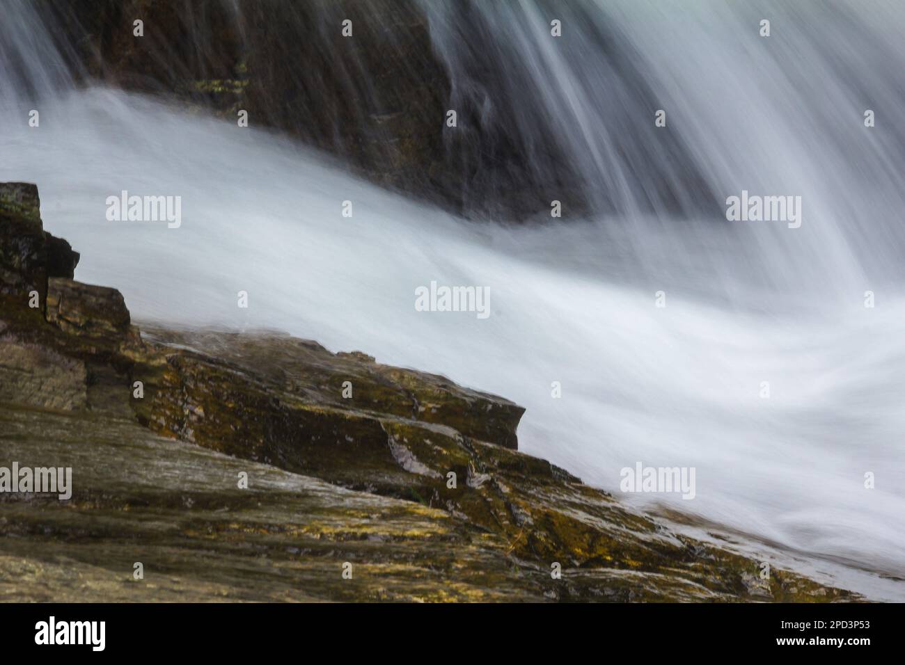 A natural waterfall flows down a long line from a cliff into a ...