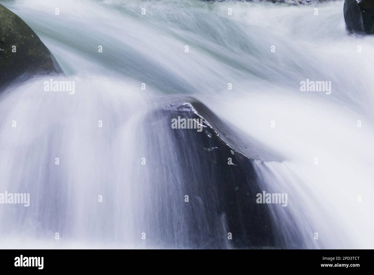 A natural waterfall flows down a long line from a cliff into a ...