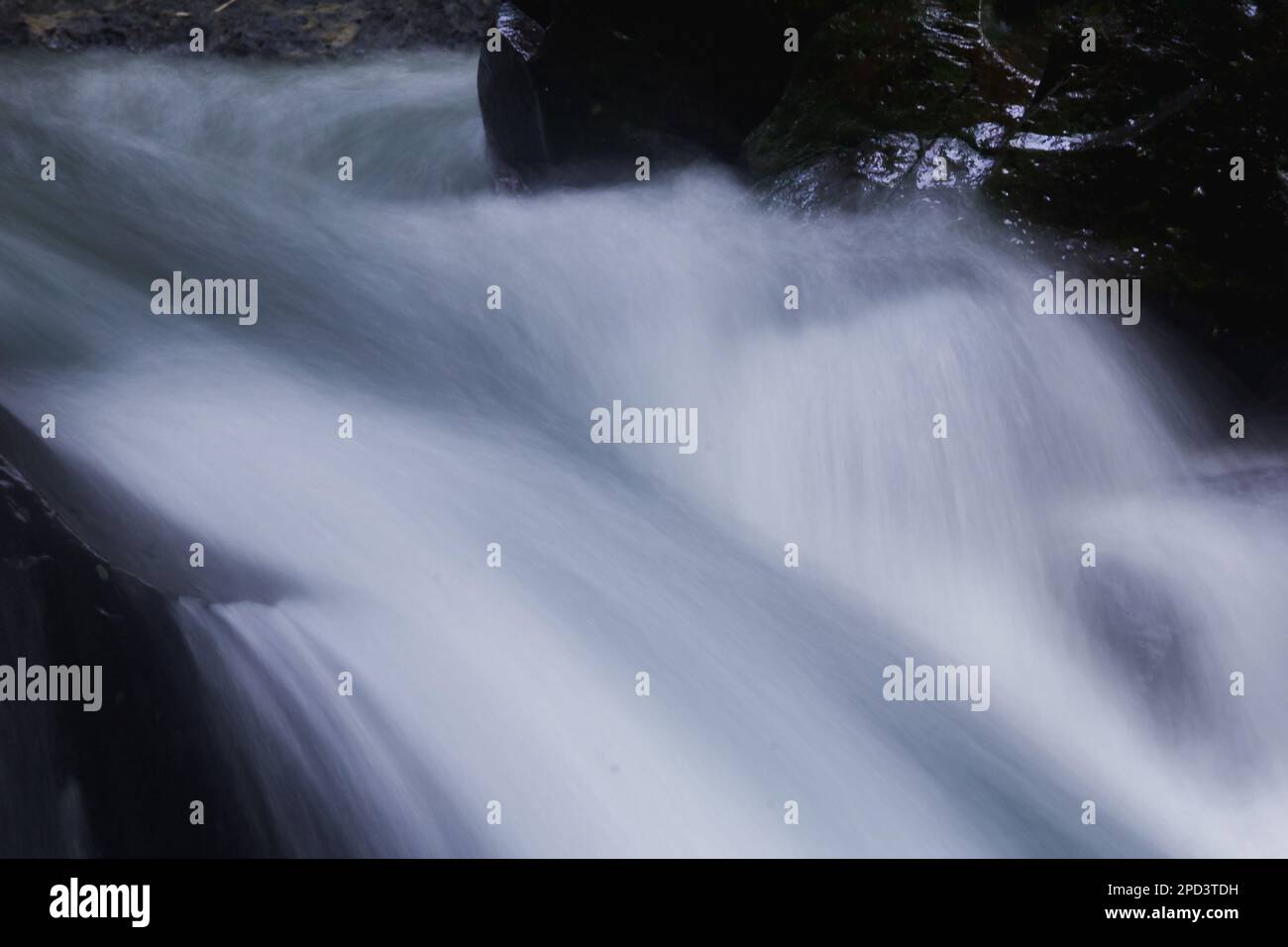 A natural waterfall flows down a long line from a cliff into a ...
