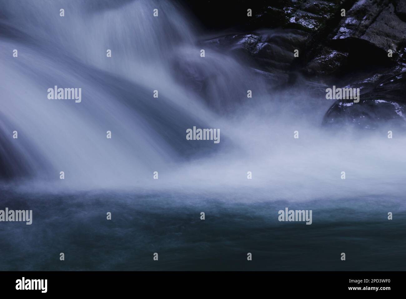 A natural waterfall flows down a long line from a cliff into a ...