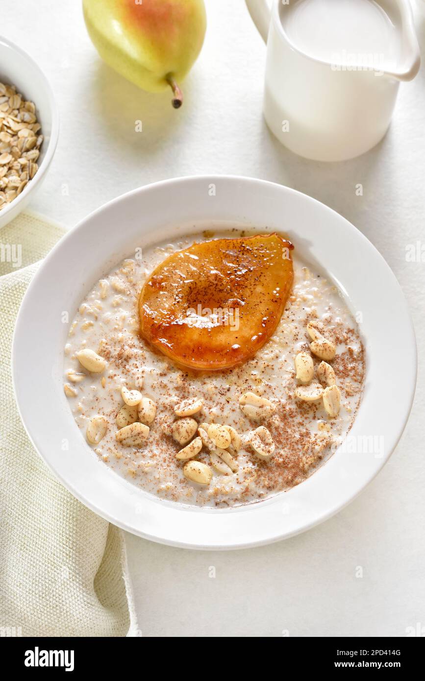 Oat porridge with caramelized pear and peanut in bowl over white ...