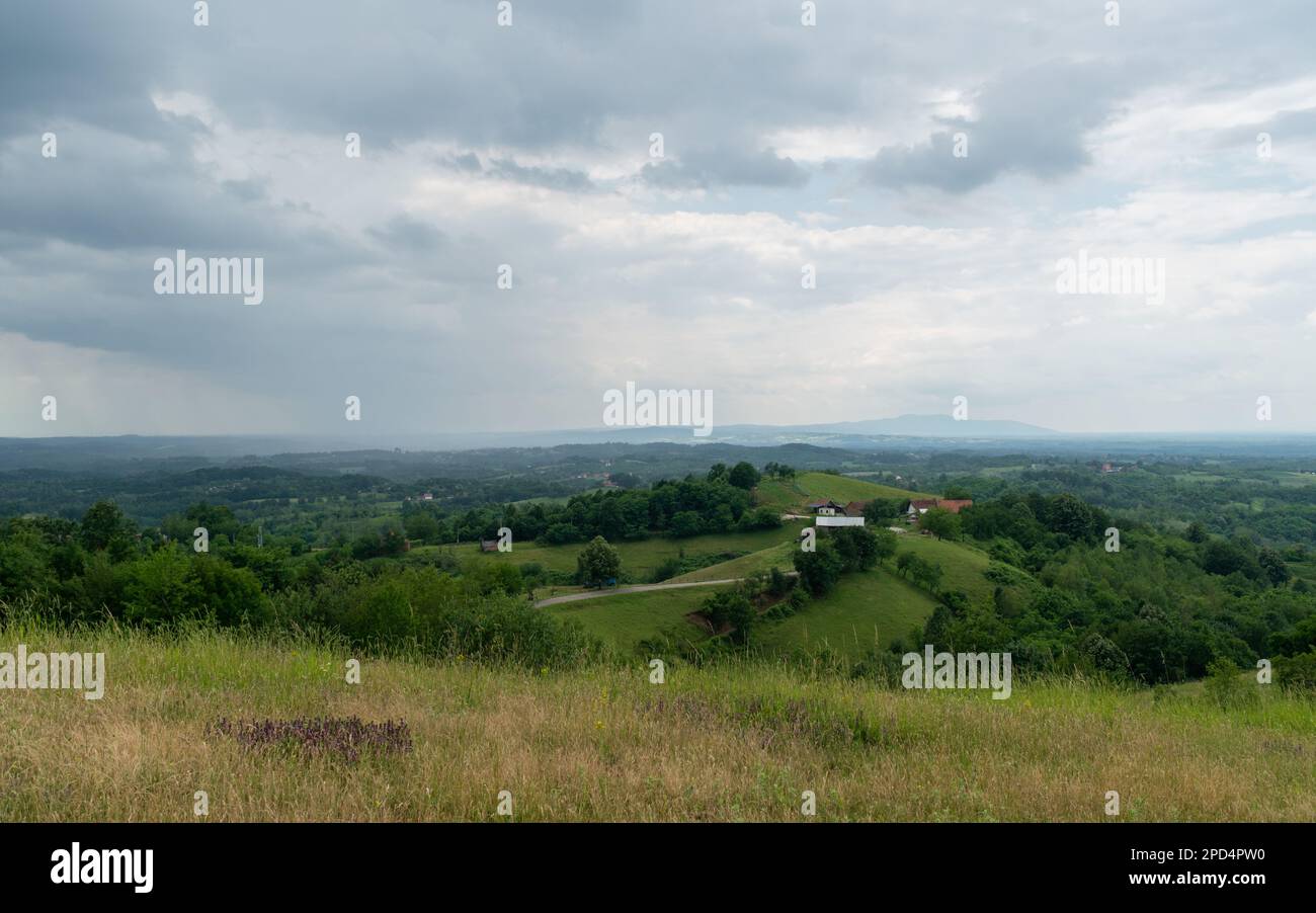 Rural landscape with farm on hill, scattered village and rainfall on ...