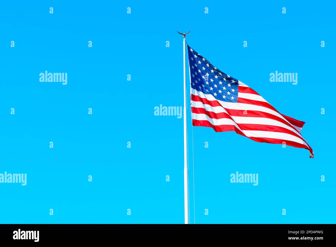 American flag on a tall flagpole flies high against a deep blue sky ...