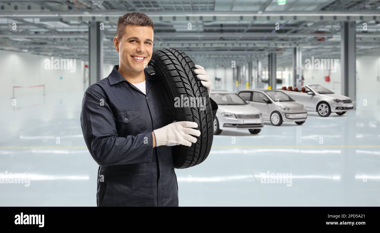 Auto mechanic worker carrying a tire on shoulder and smiling at camera ...