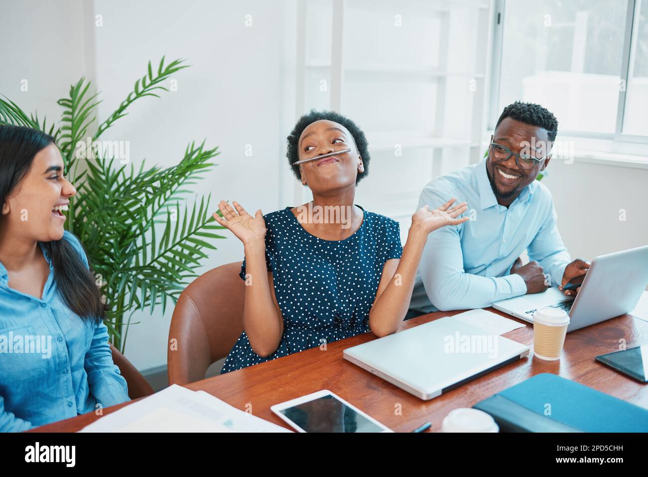 Young woman entertains her colleagues in office, pulling silly fun face ...