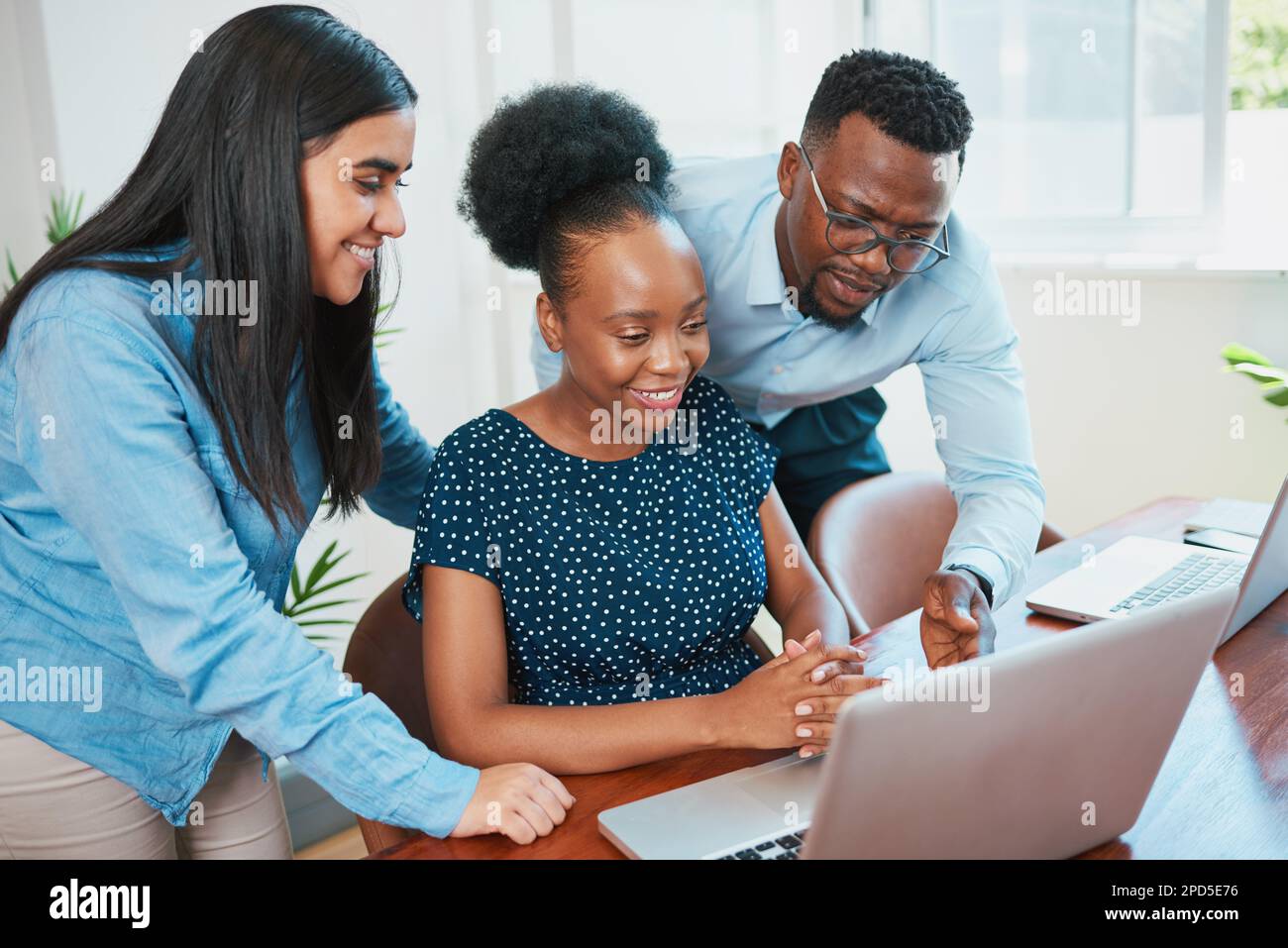 Three diverse colleagues discuss and laugh around laptop in office ...