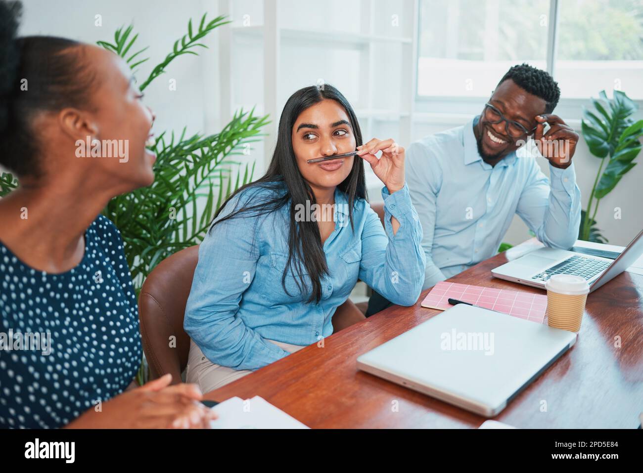 Young woman entertains her colleagues in office, pulling silly fun face ...