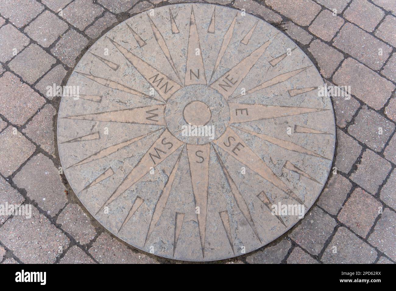 A stone plaque of the compass points on the pavement in the town square ...