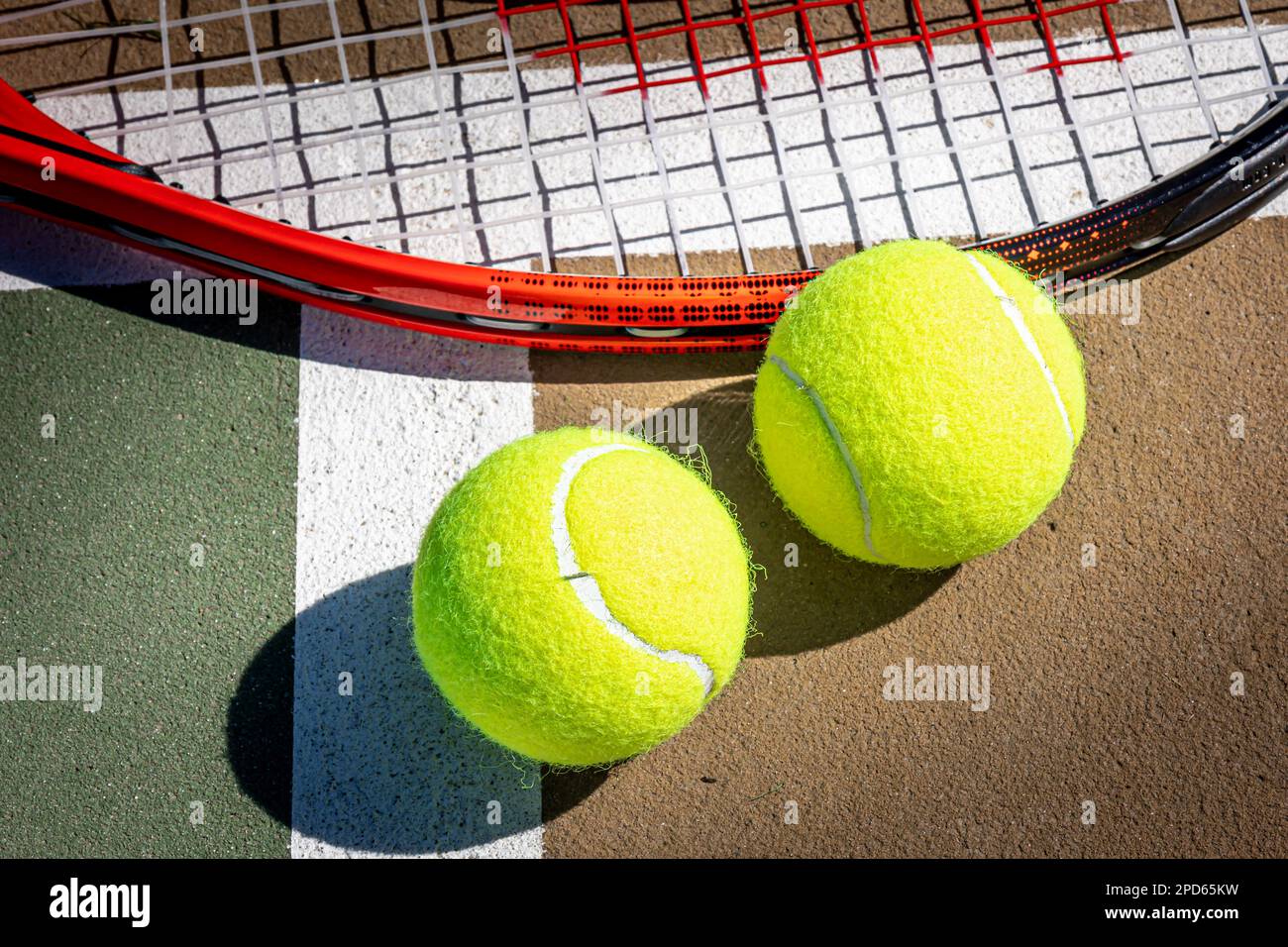 A red and a blue tennis racket with two tennis balls on the surface of ...