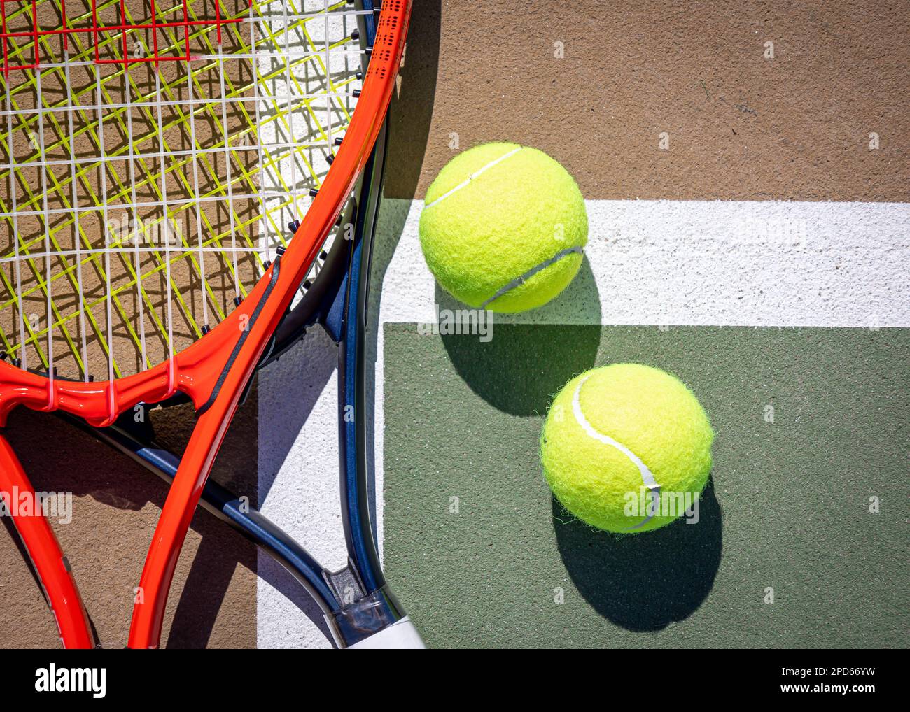 A red and a blue tennis racket with two tennis balls on the surface of ...