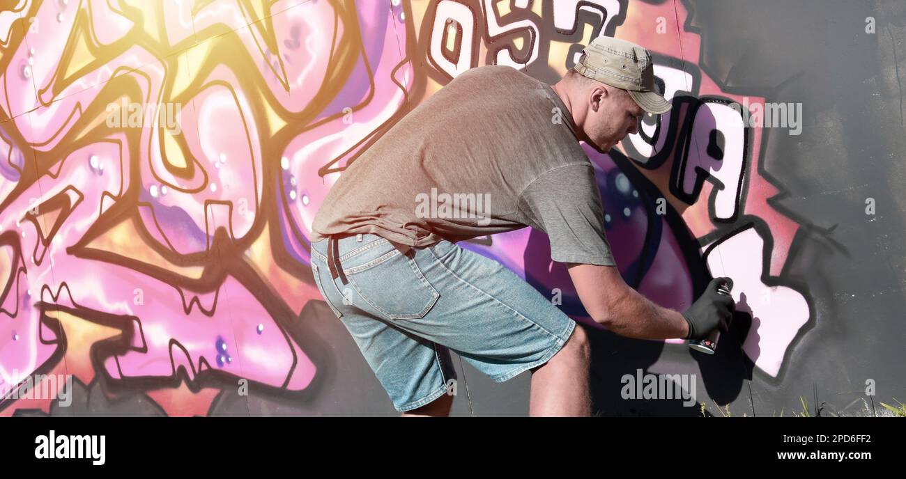 Young caucasian male graffiti artist drawing big street art painting in ...