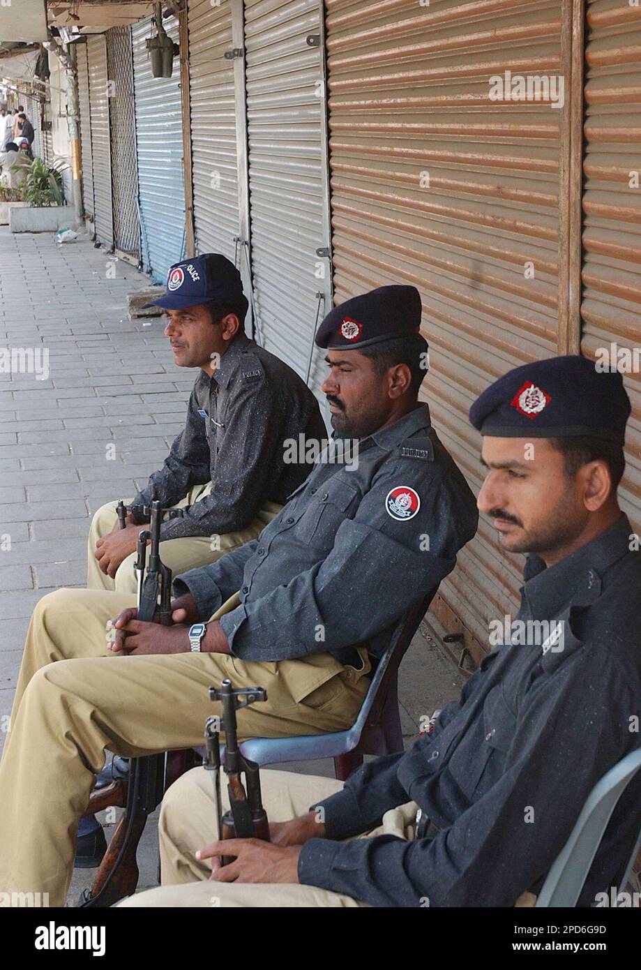 Pakistani police officers sit in front of shops, which closed due to a ...