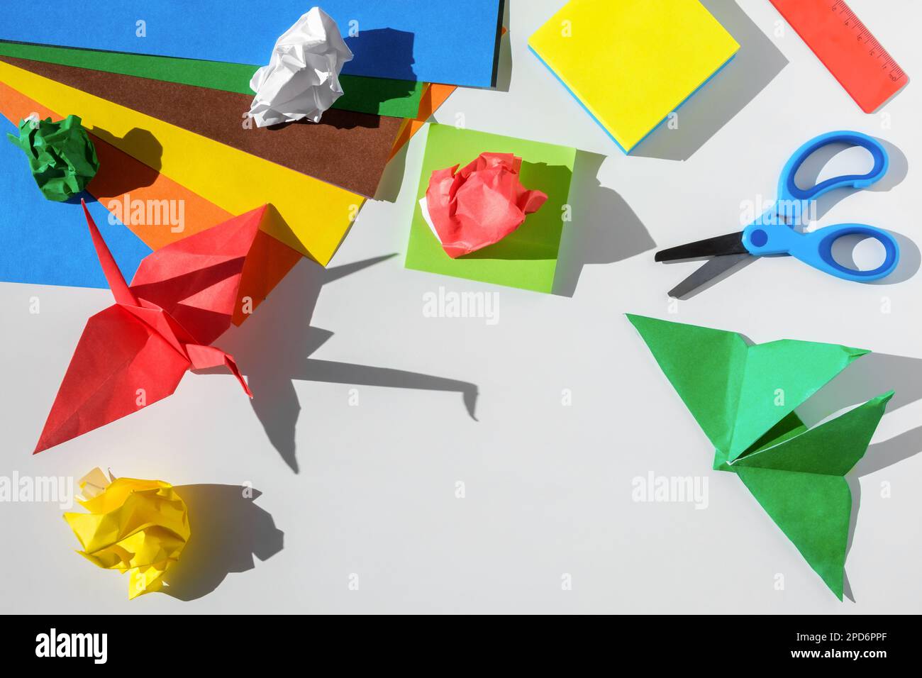 Paper crafts, scissors, colored paper sheets and scraps, on white table ...