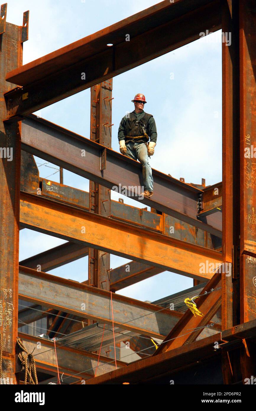 A construction worker stands on a steel beam while working on a high ...