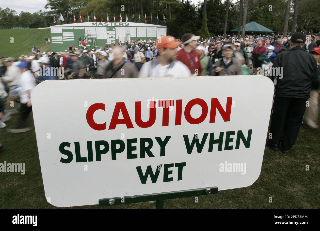 Masters patrons walk past a "Slippery When Wet" sign as they enter the ...