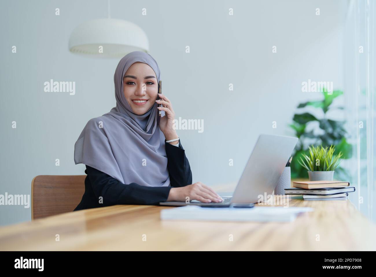 Beautiful Muslim woman talking on the phone and using a computer on her ...