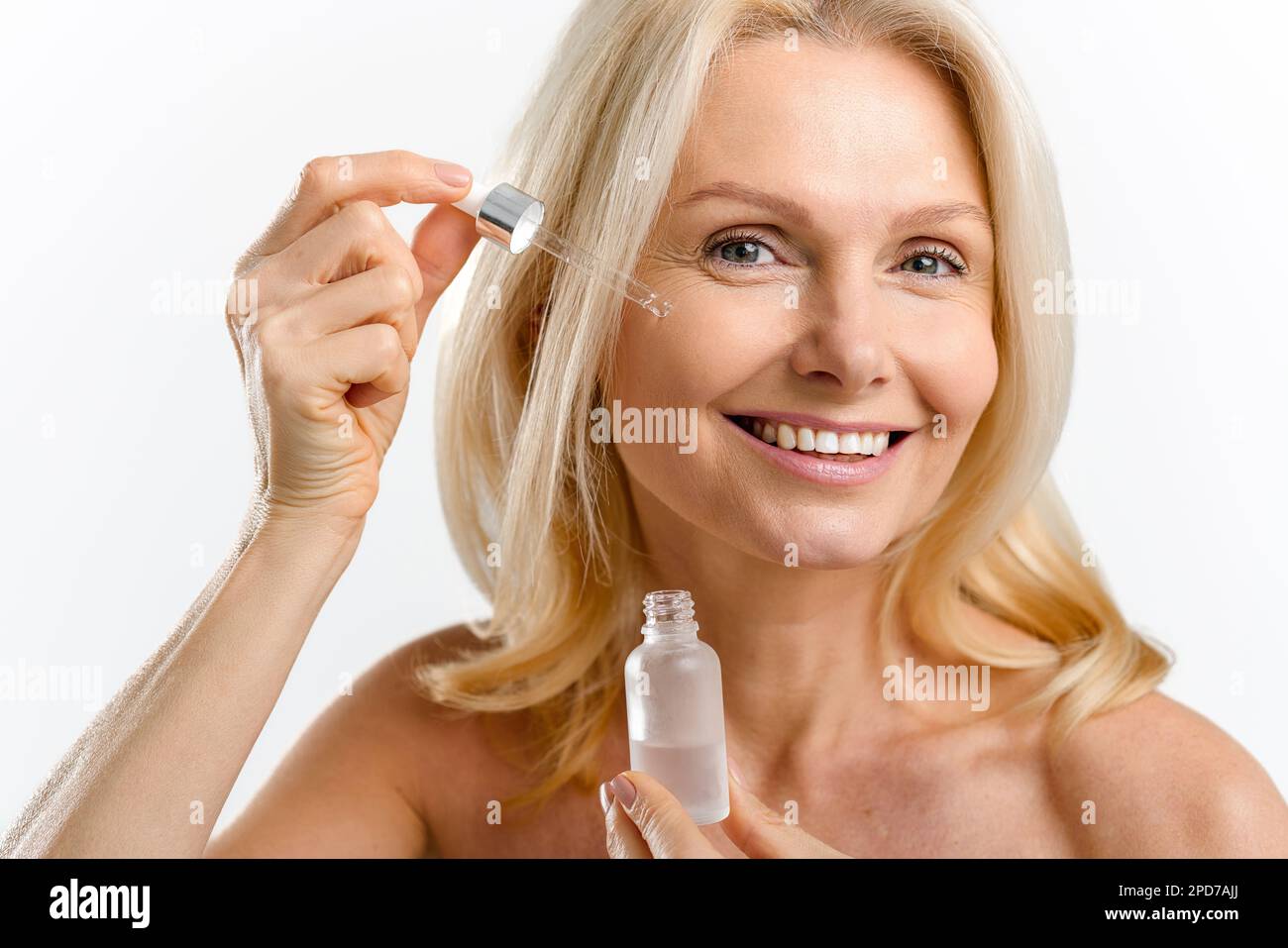 Close-up portrait of magnificent middle-aged blonde woman using skin ...