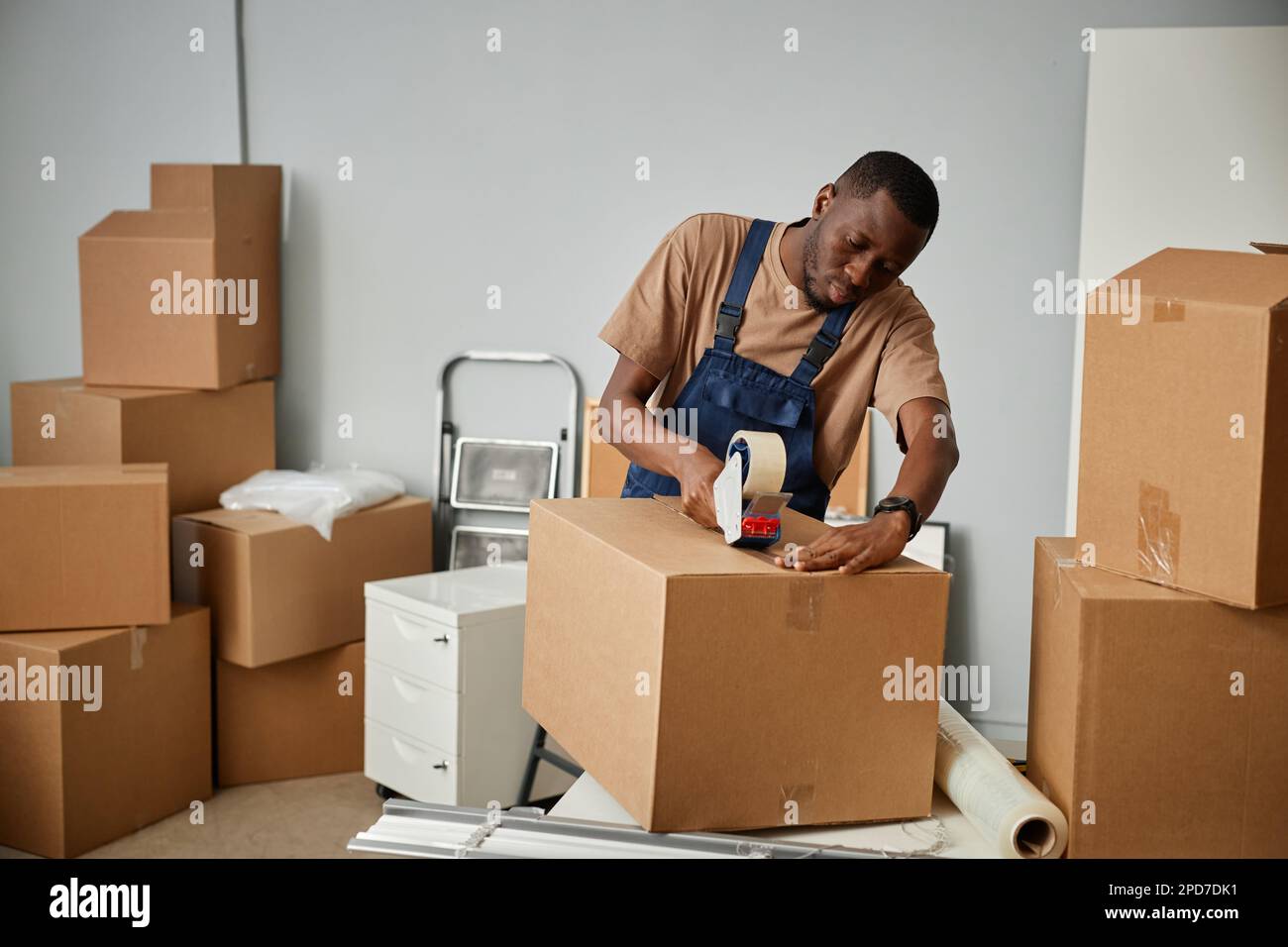 African American worker packing boxes with adhesive tape during ...