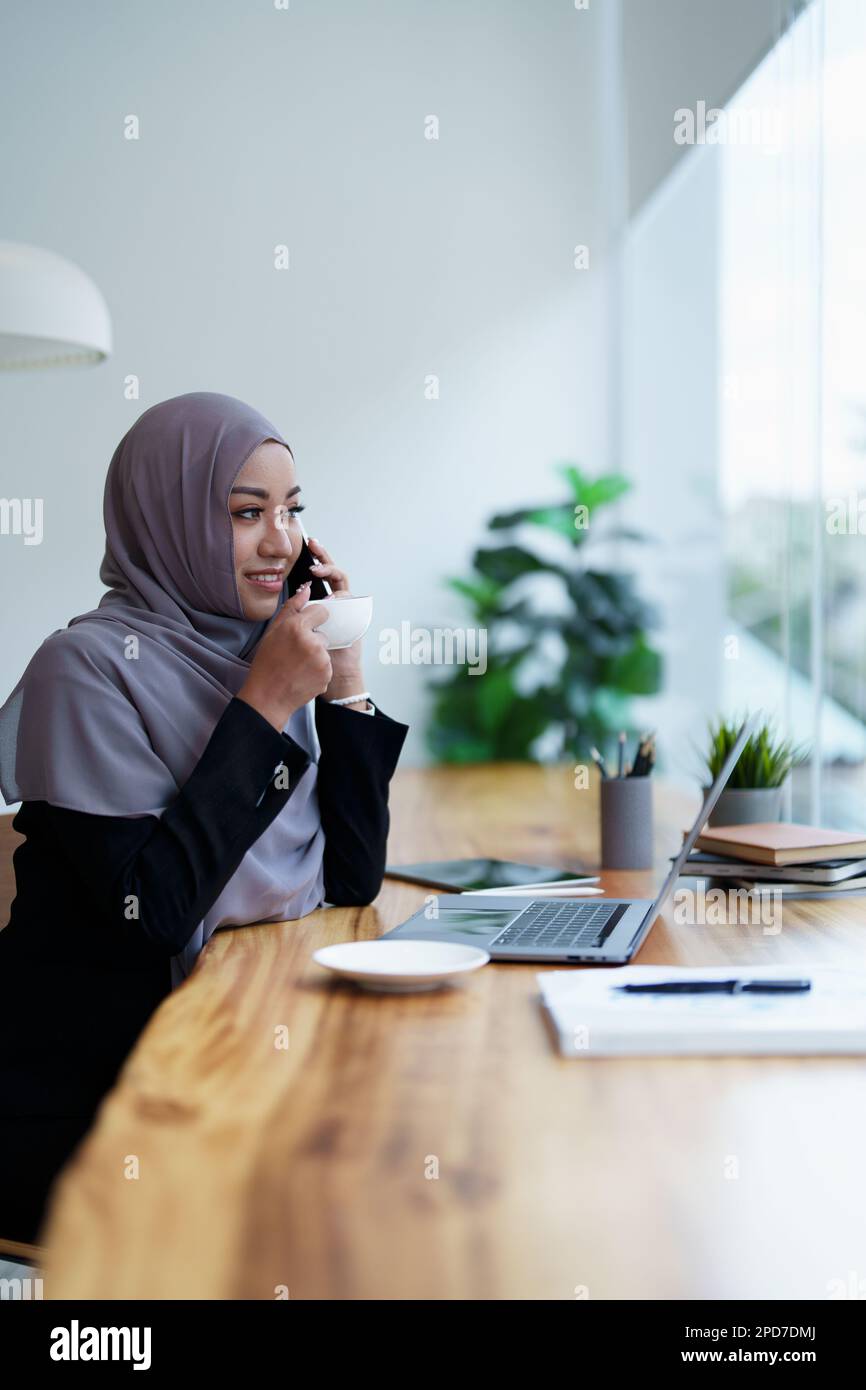 Beautiful Muslim woman talking on the phone and using computer on top ...