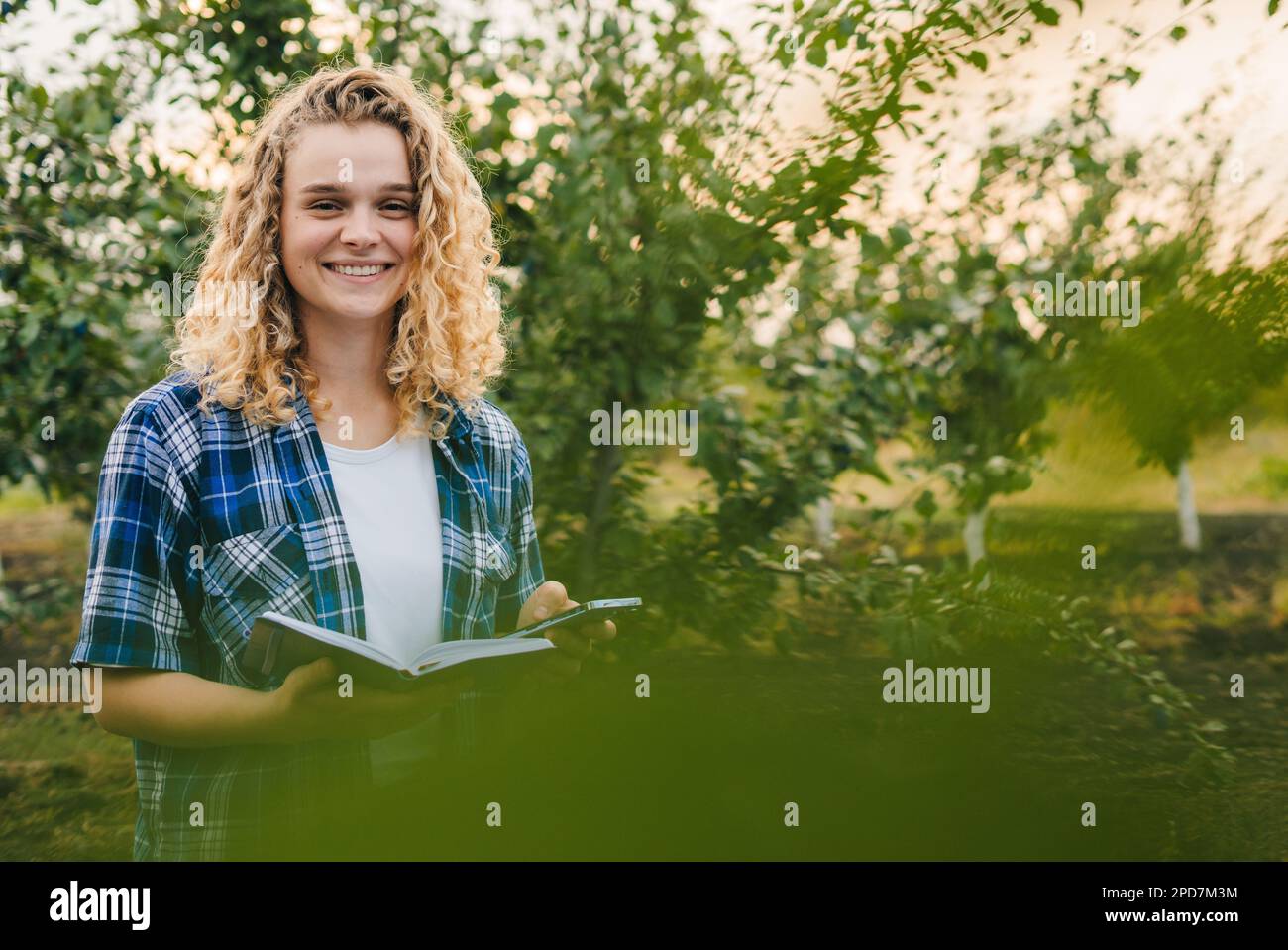 Curly-haired woman farmer writing notes on clipboard notepad in organic ...