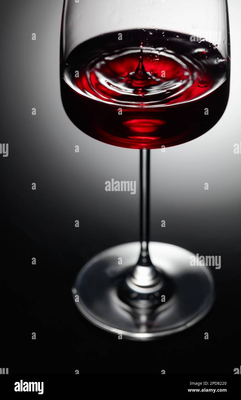 The drop of red wine falls into a wine glass. Black background ...