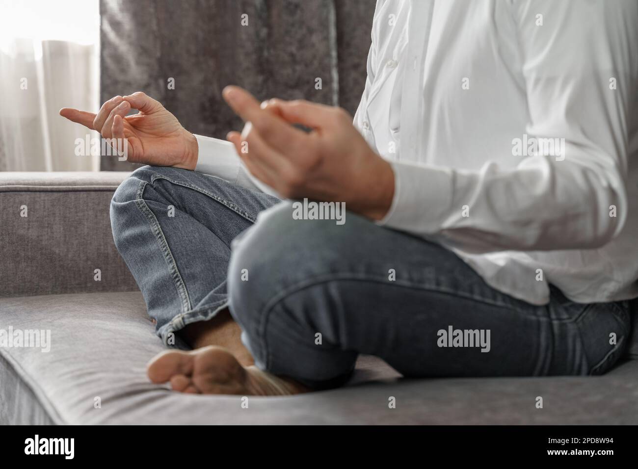 Close-up of a man sitting on a sofa in the lotus position. Close-up ...