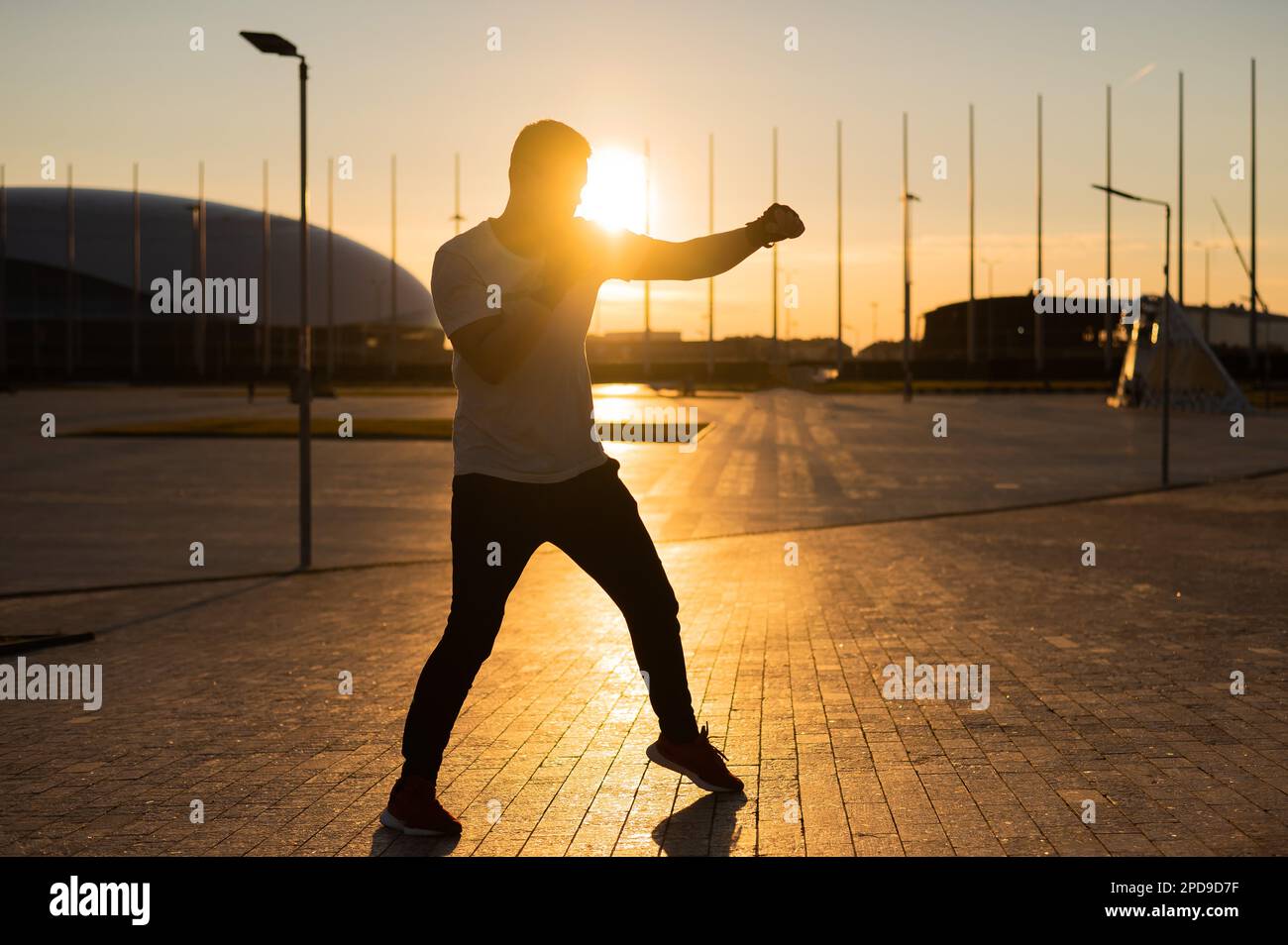 A man trains in boxing at the stadium at sunset. Athlete silhouette ...