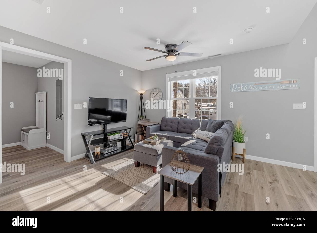 A modern light-colored room with large windows, a sleek grey sofa, and ...