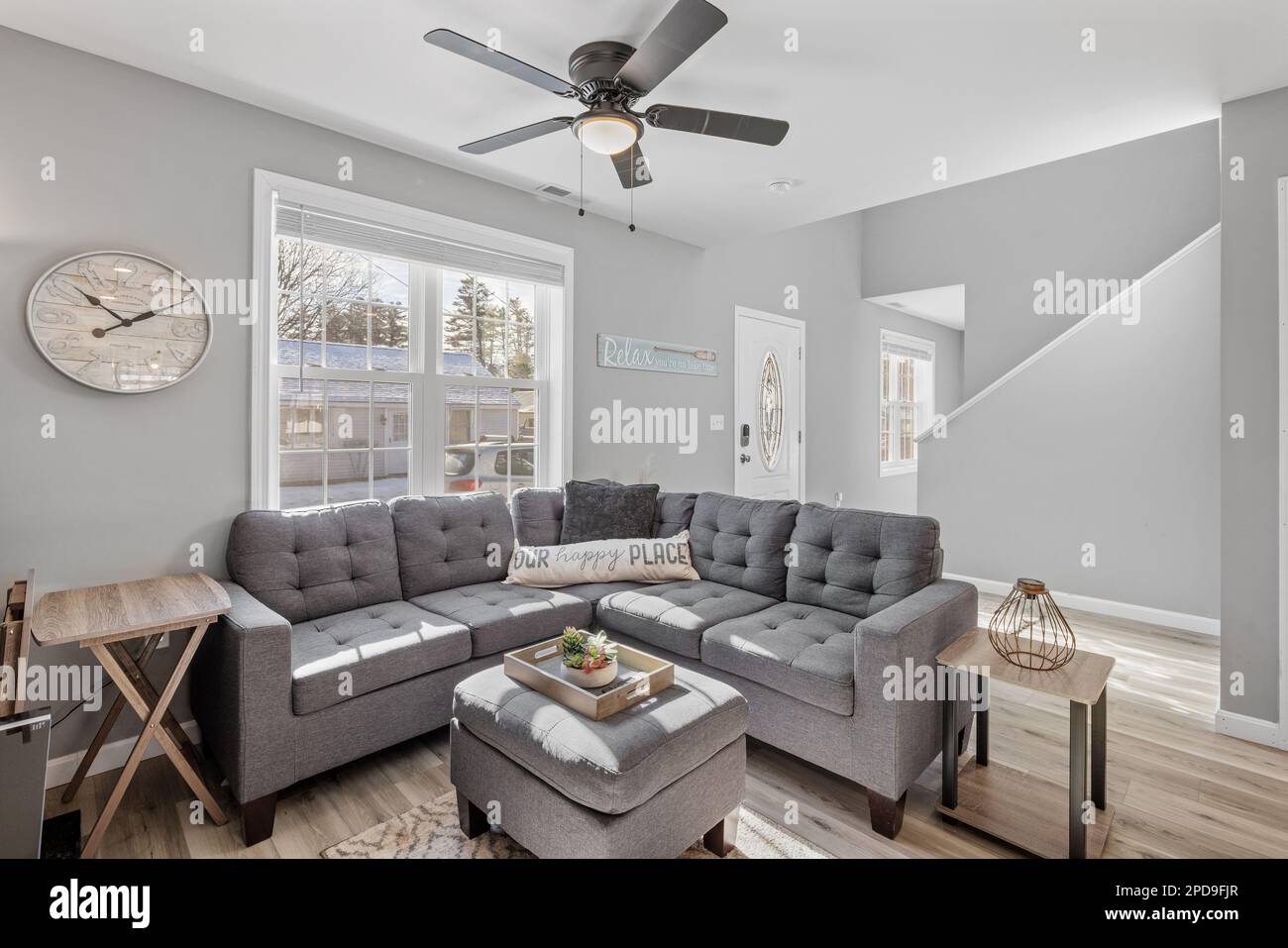 A modern light-colored room with large windows, a sleek grey sofa, and ...