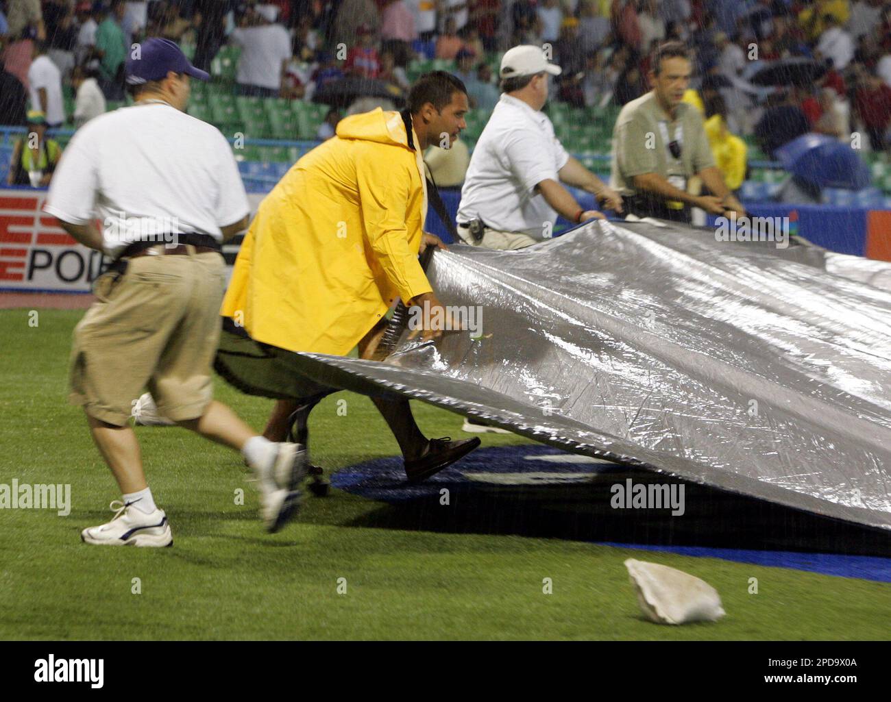 Grounds crew workers pull a tarp over the playing field as rain falls ...