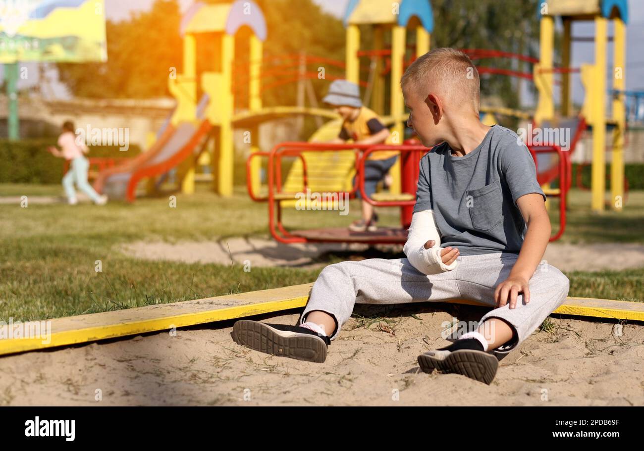 crying child with broken limb arm sits outdoors and looking how kid ...