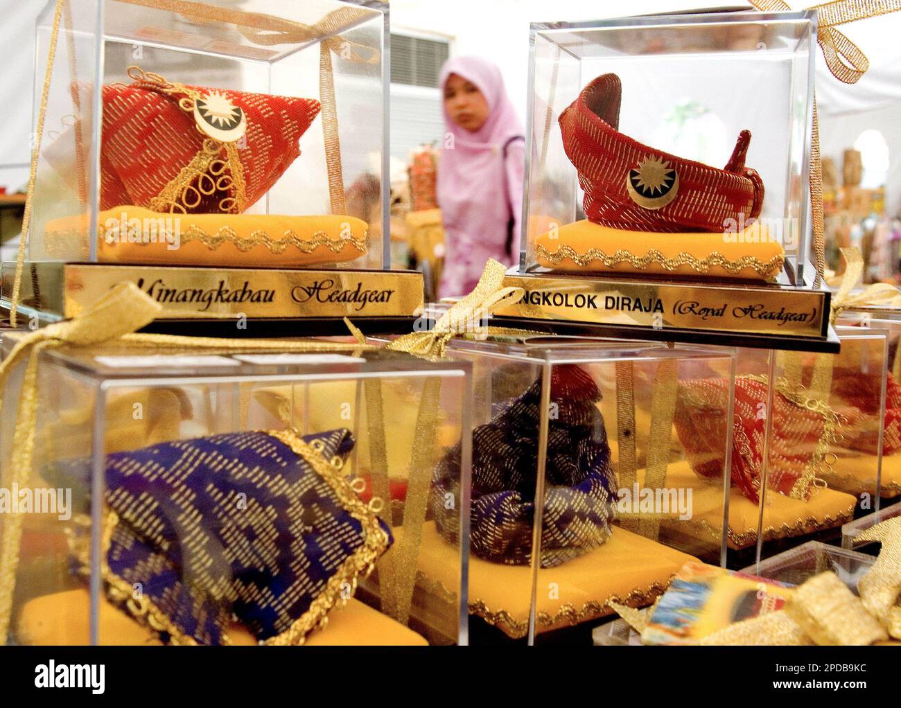 A Muslim woman walks past miniature handmade Malays headdresses on ...