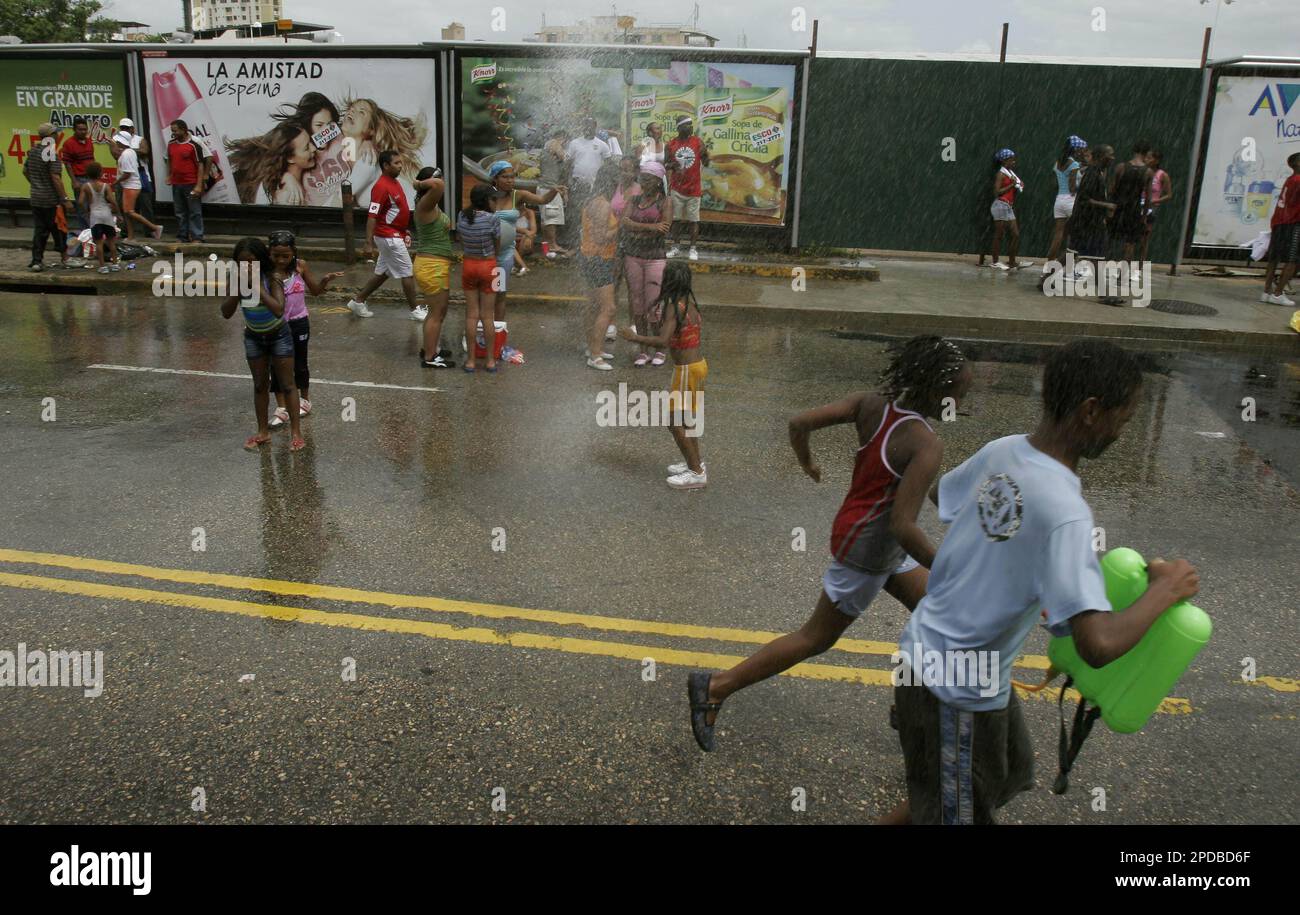 Children run in the street as cars spray them with water during a ...