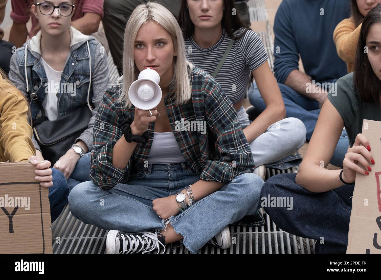Young multicultural students sit on a street in protest holding signs ...