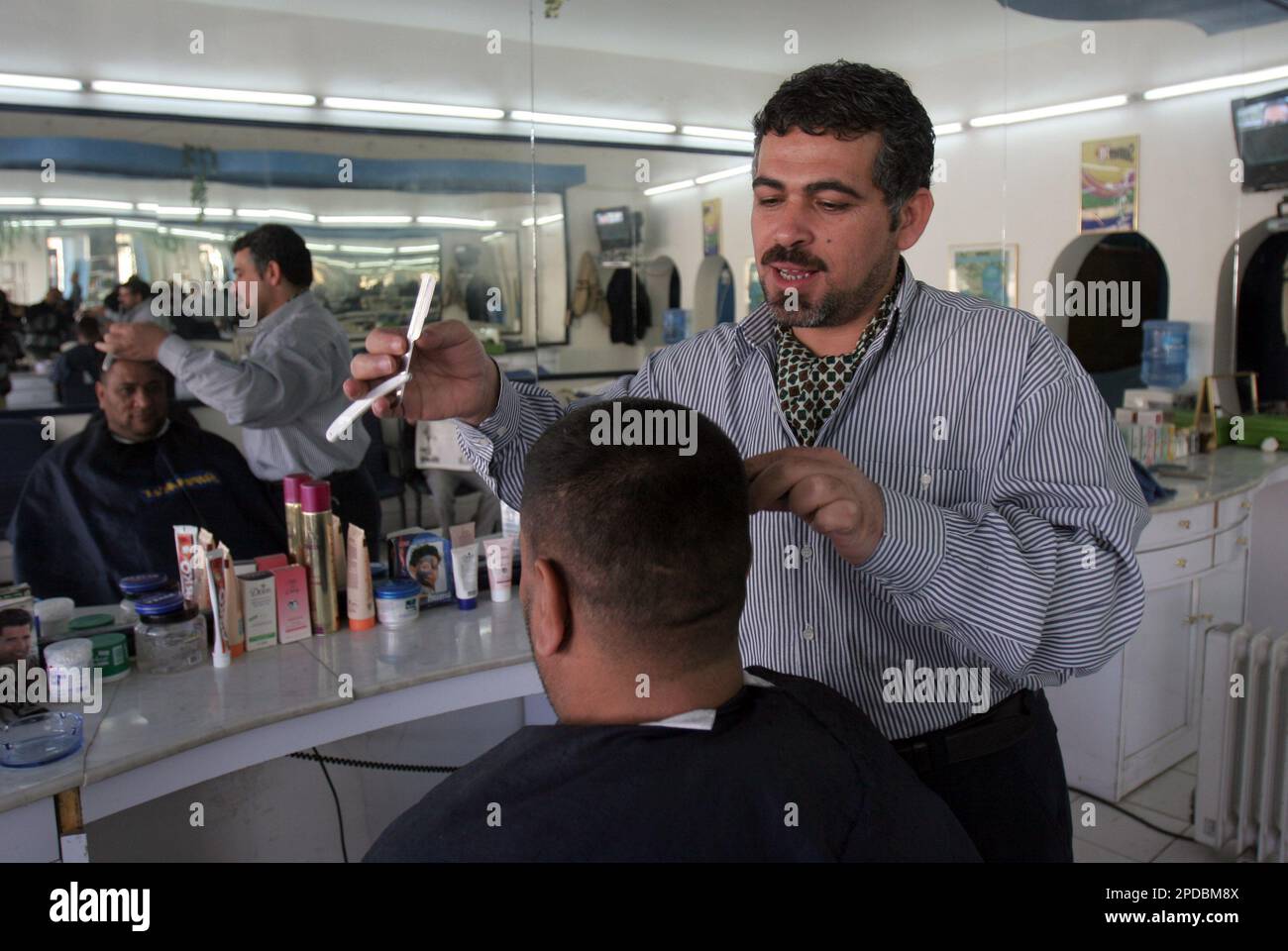 Qais al-Sharaa gives a haircut to a customer in his barber shop in ...