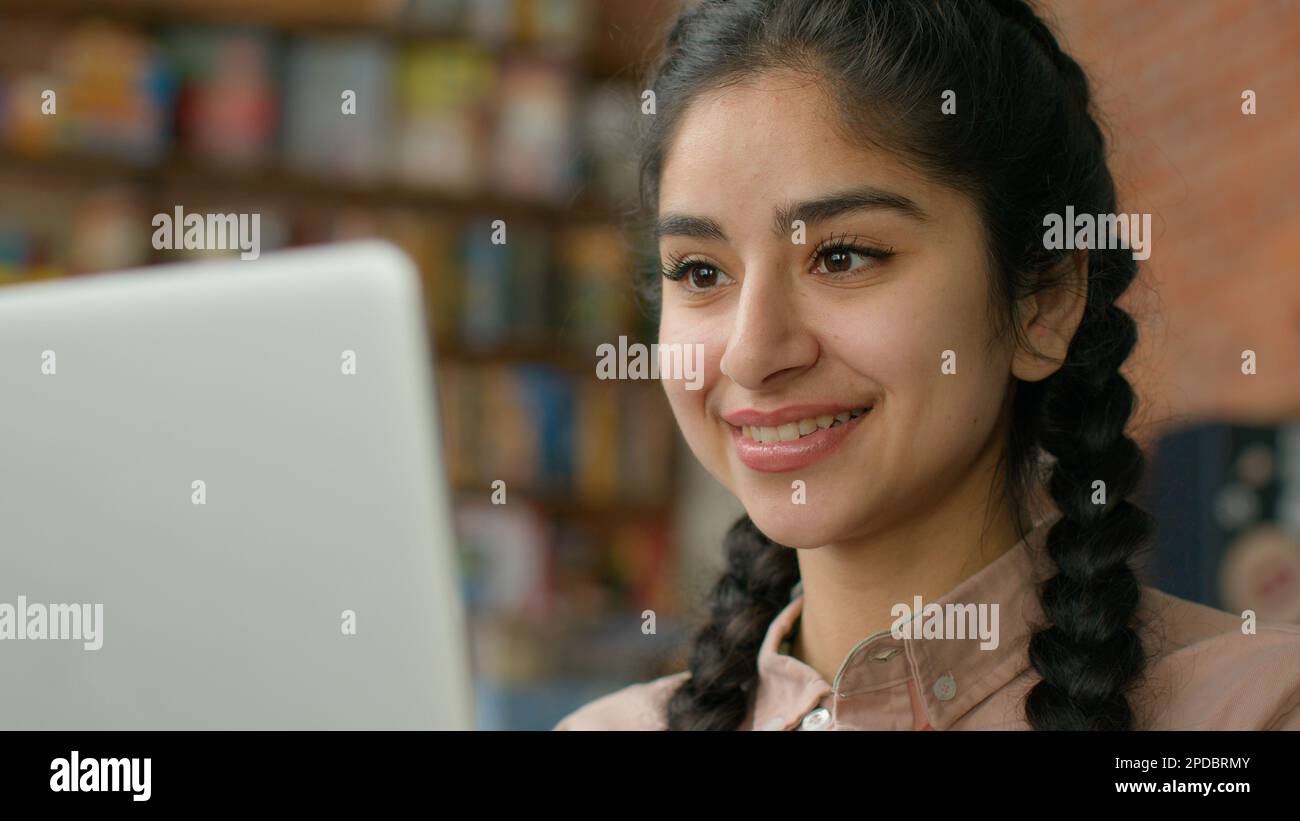 Close-up smiling young indian woman looking at laptop screen indoors ...