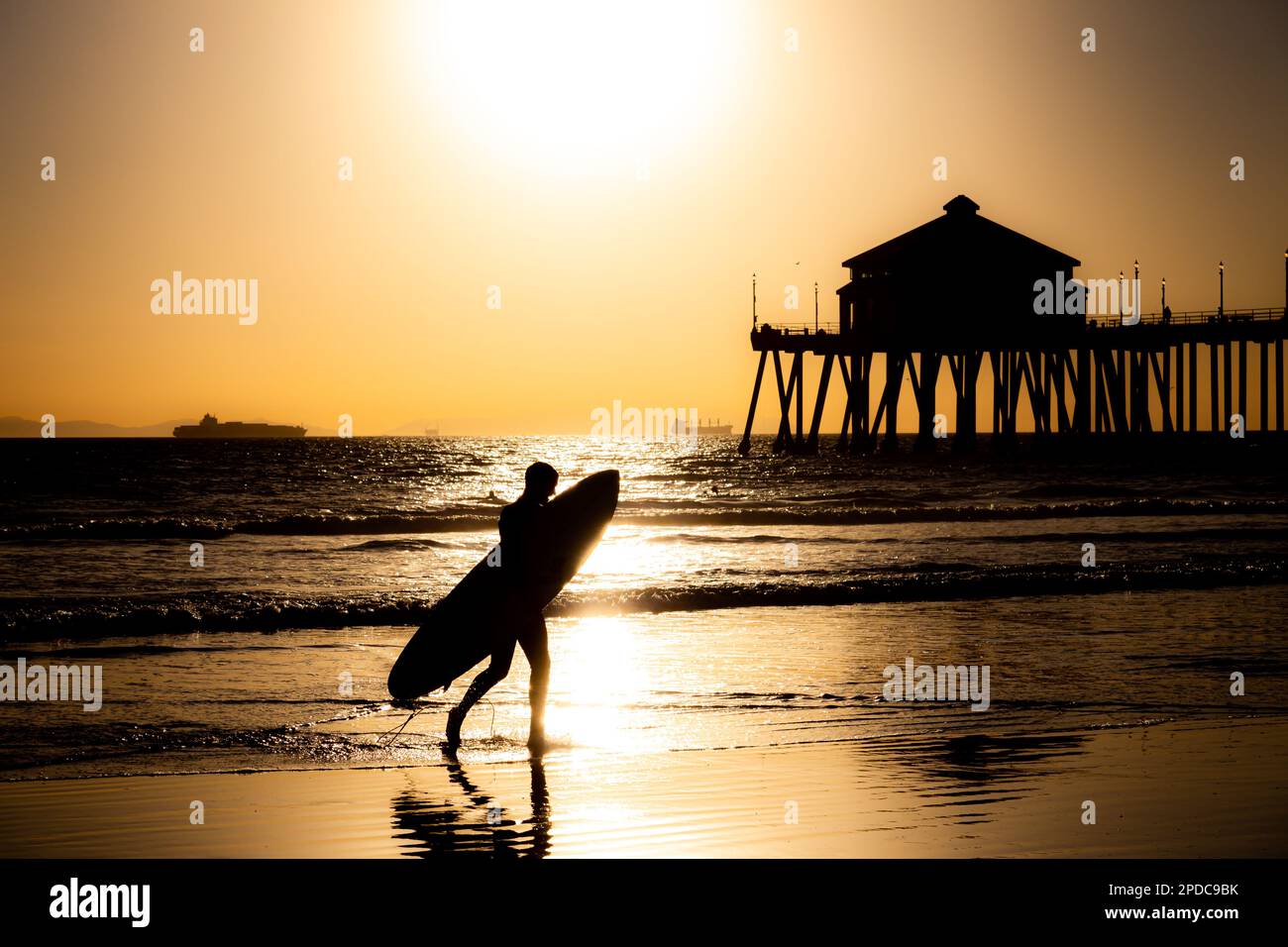 Silhouette of a surfer walking on the beach carrying a surfboard in ...