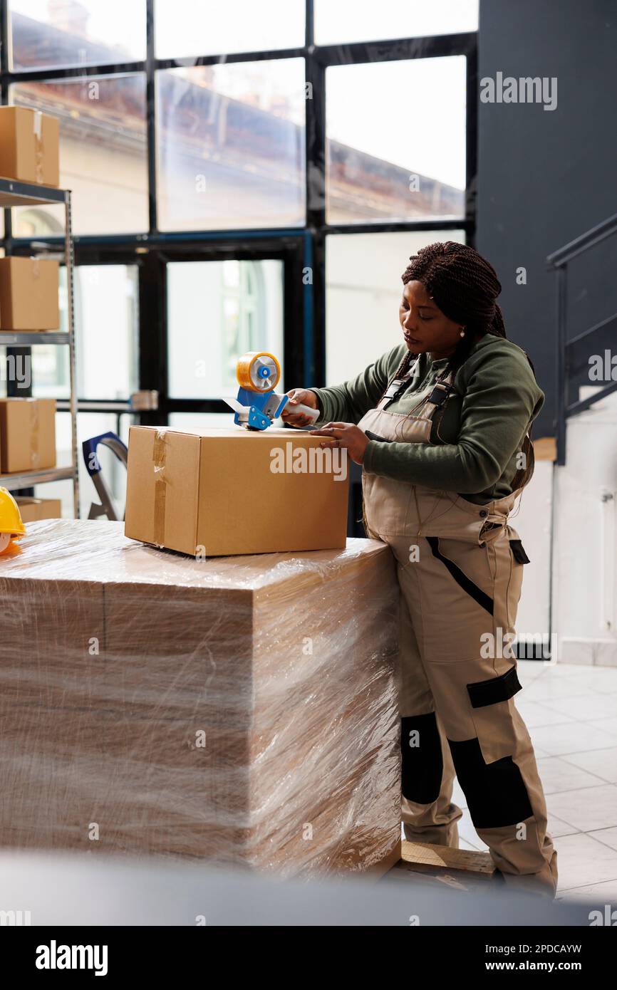 Employee putting adhesive tape on cardboard boxes, preparing customers ...