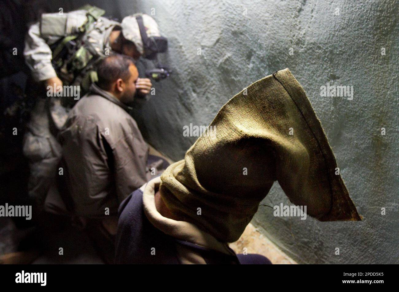 An Iraqi detainee sits with his head covered by a sand bag while an ...