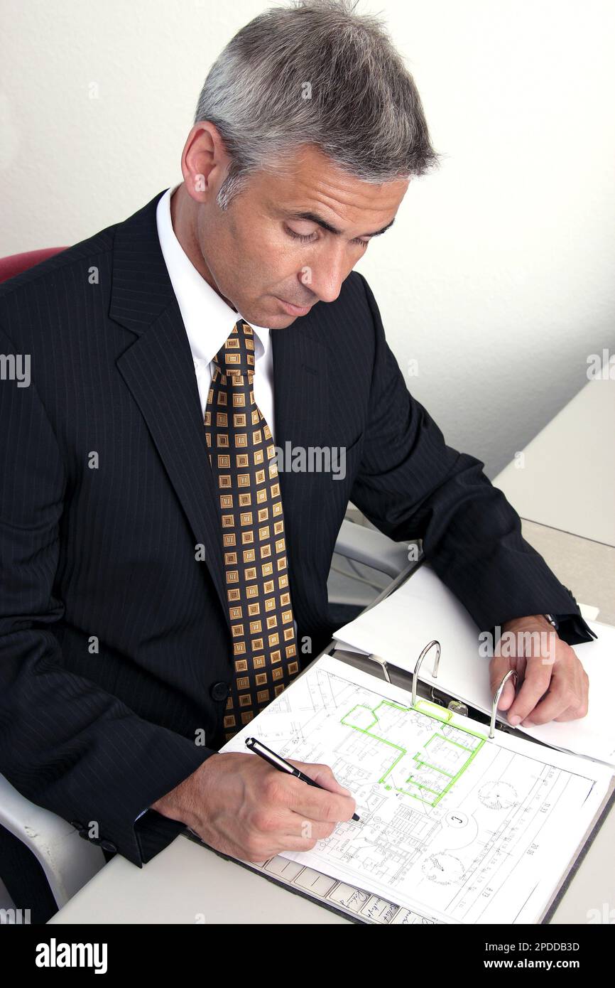 architect sitting at a desk and making notes in a construction drawing ...