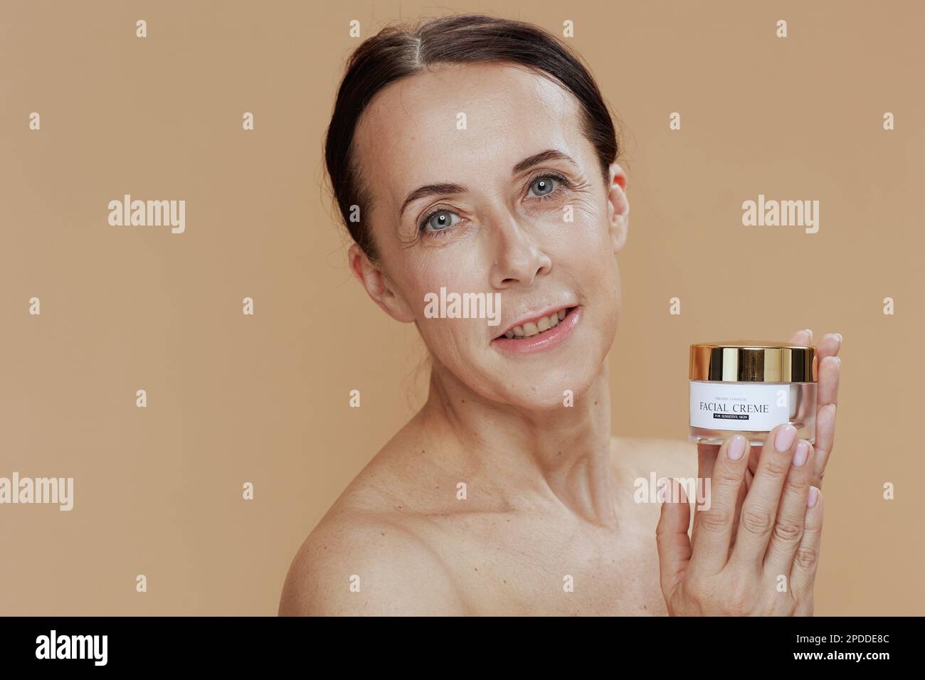 Portrait of modern middle aged woman with facial cream jar on beige ...