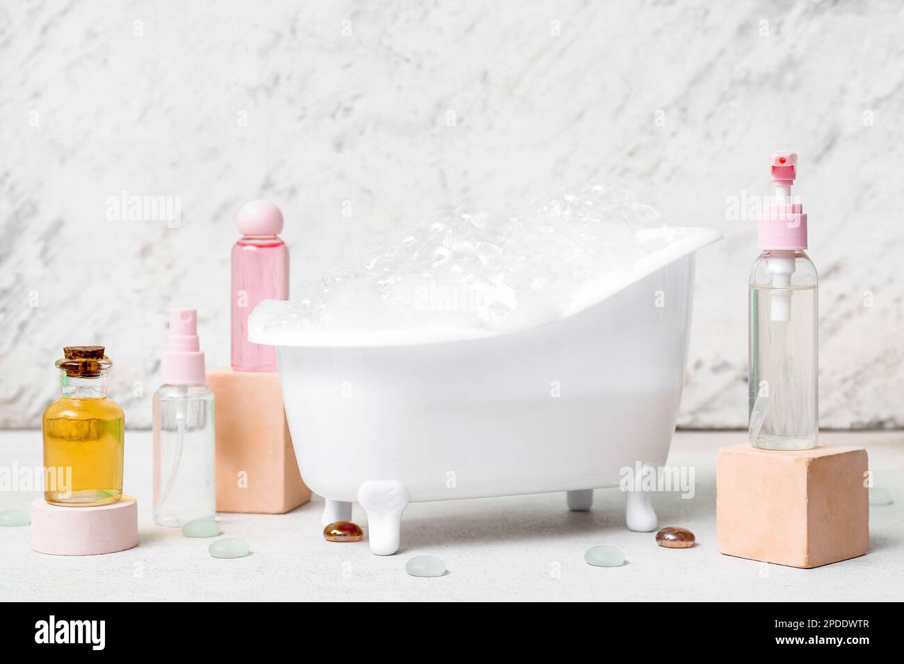 Small bathtub with foam and bottles of cosmetic products on light ...