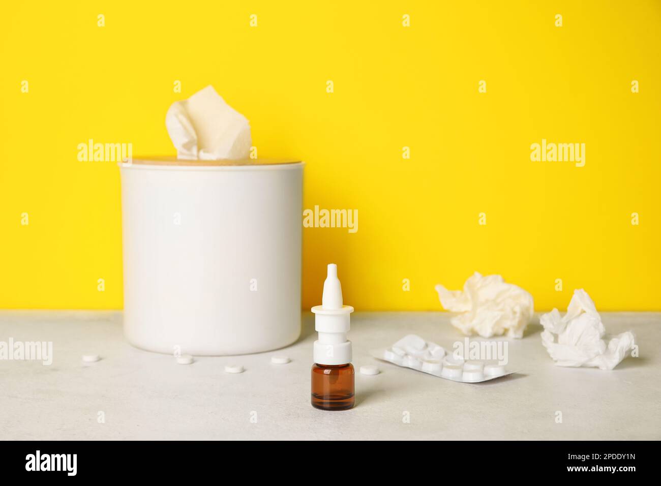 Nasal drops with pills and tissue box on table near yellow wall ...