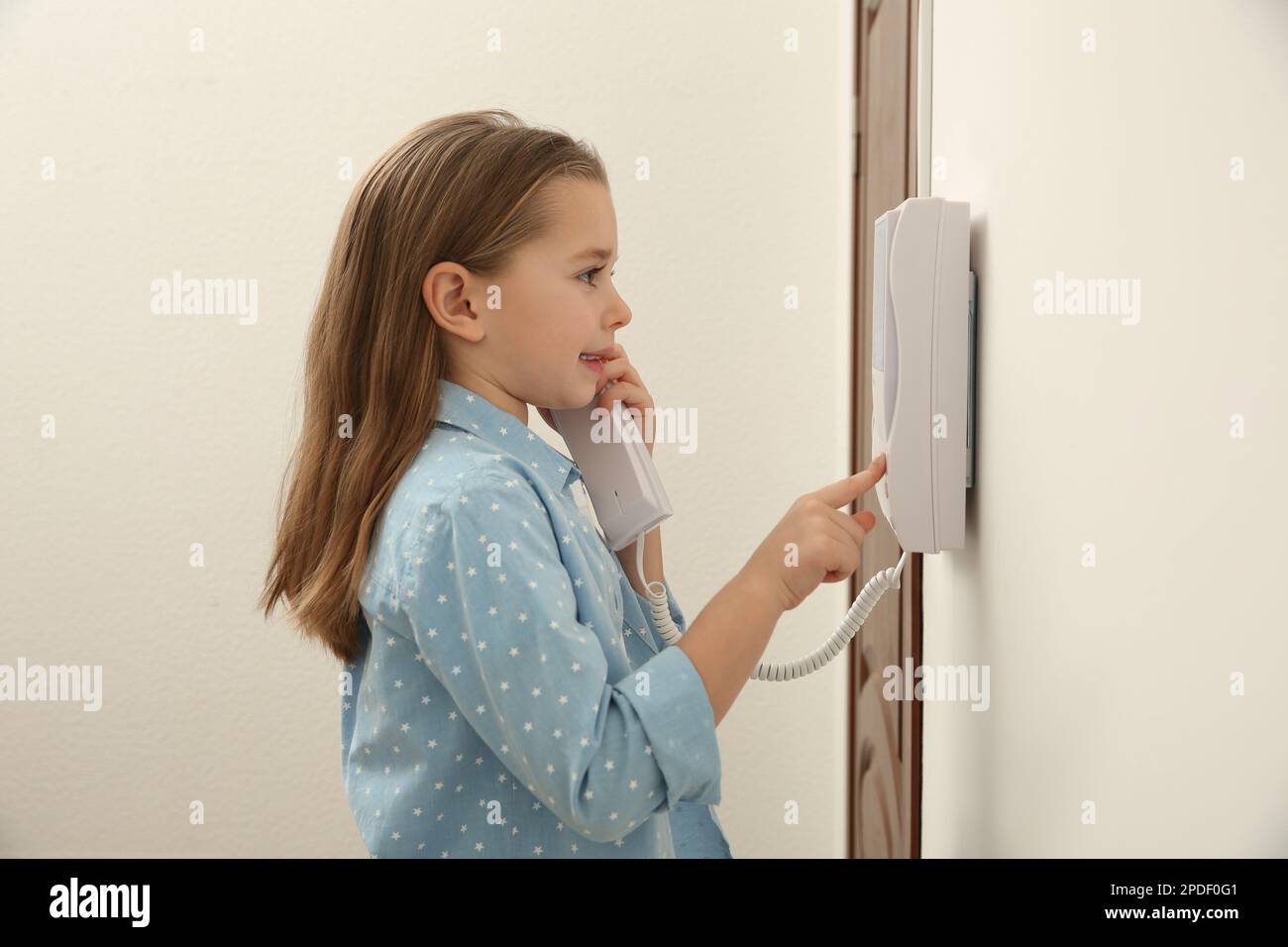 Cute little girl answering intercom call indoors Stock Photo - Alamy
