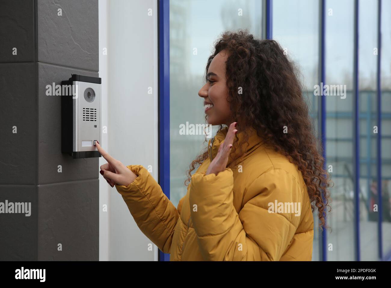Young African-American woman ringing intercom while waving to camera ...