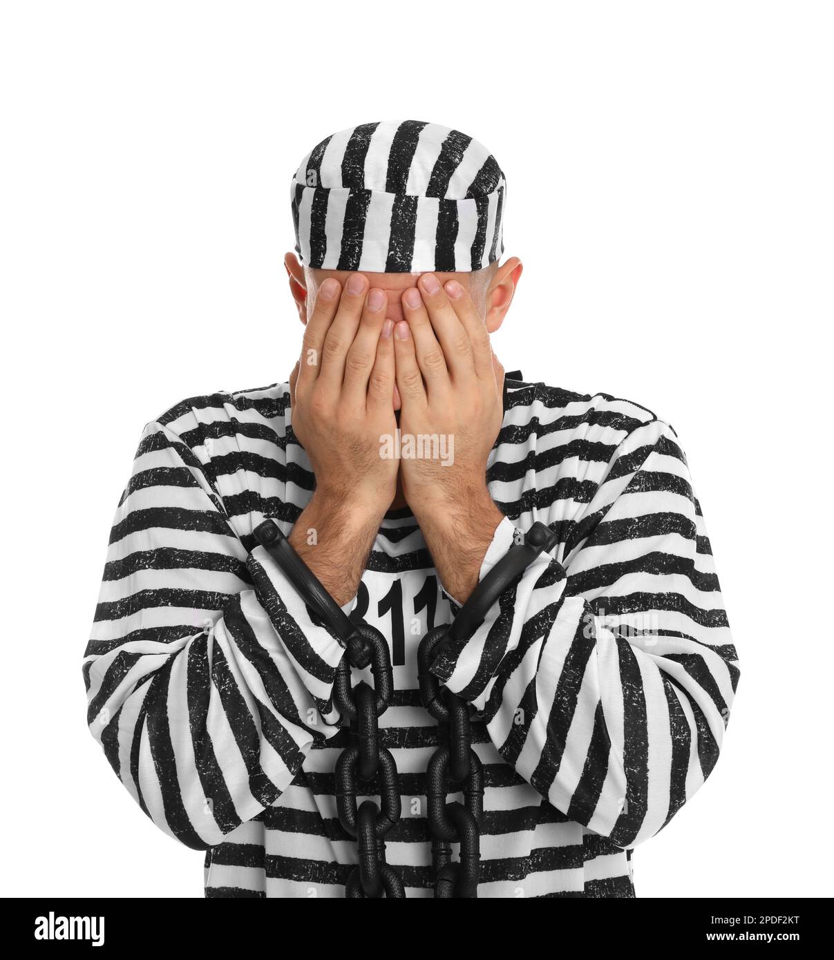 Remorseful prisoner in striped uniform with chained hands hiding his ...
