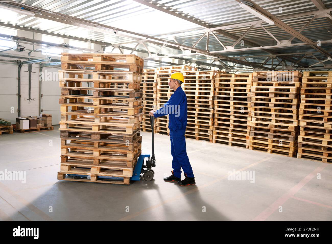 Worker moving wooden pallets with manual forklift in warehouse Stock ...
