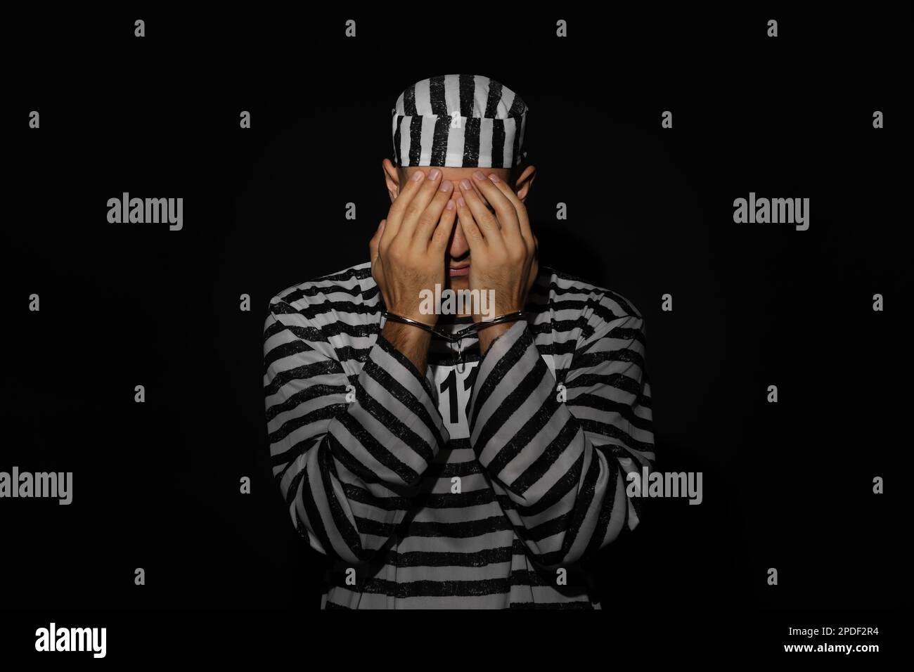 Remorseful prisoner in striped uniform with handcuffs hiding his face ...