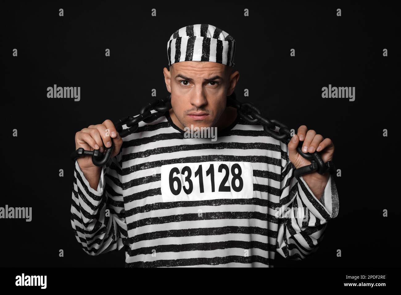 Prisoner in striped uniform with chained hands on black background ...